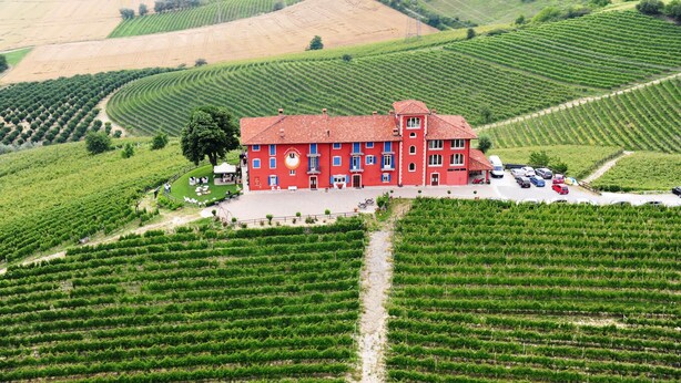 Um edifício vermelho com telhado em telhas, rodeado por vinhedos em socalcos.