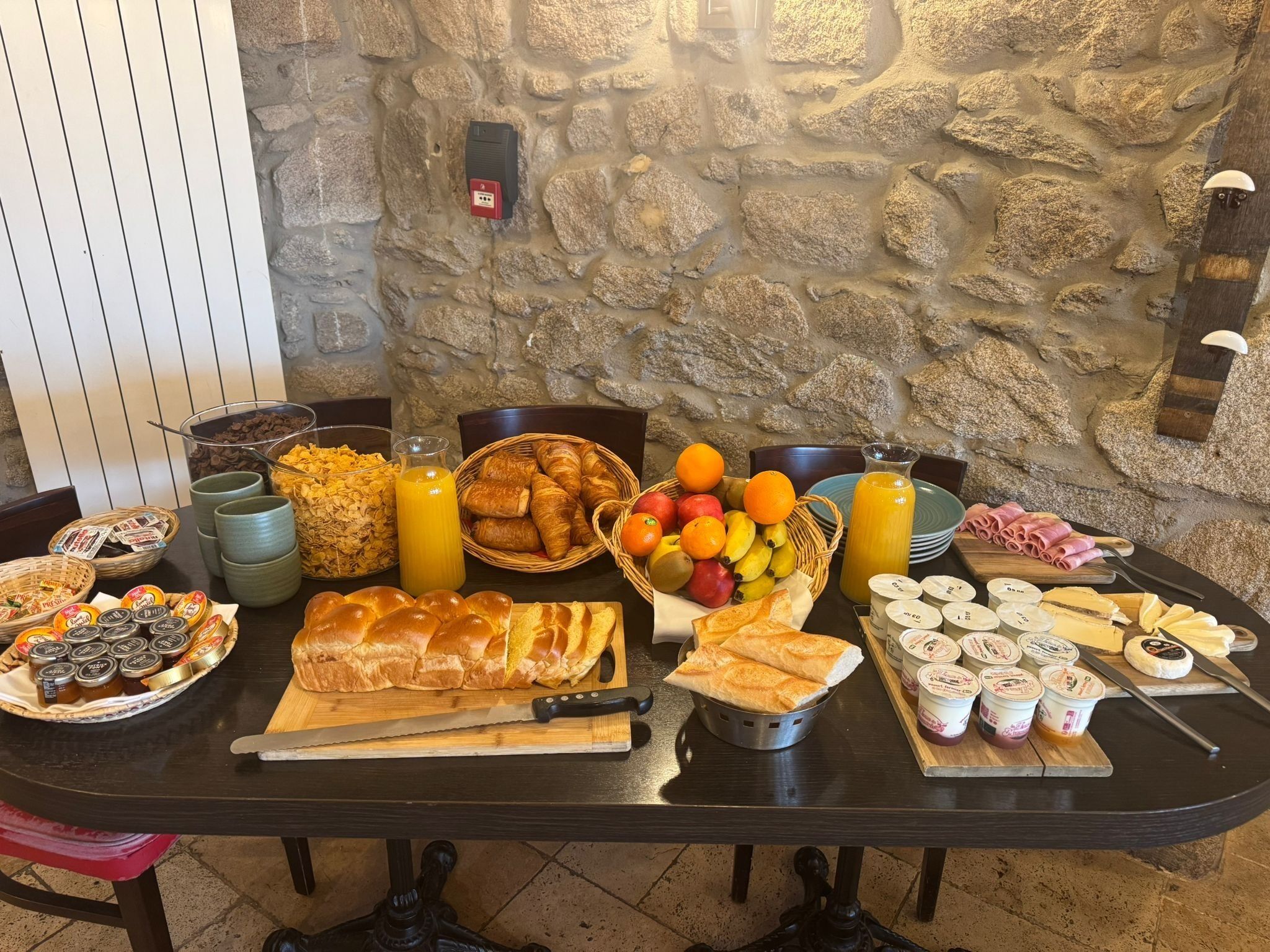 Buffet de café da manhã com diversos alimentos e um fundo de parede de pedra.