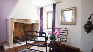 Quarto com lareira, duas cadeiras, uma mesa com um vaso de flores e uma janela com cortinas.