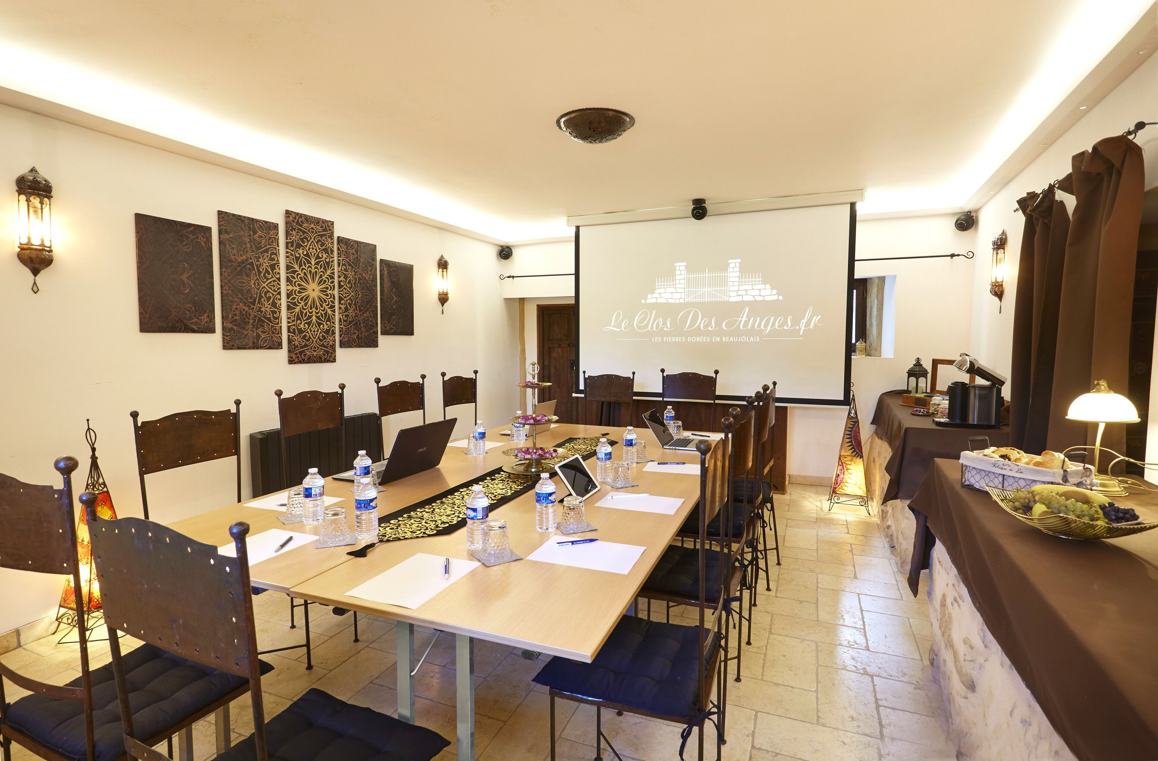 Uma sala de conferências com uma mesa comprida, cadeiras, laptops, garrafas de água e uma tela de projetor exibindo um logotipo.