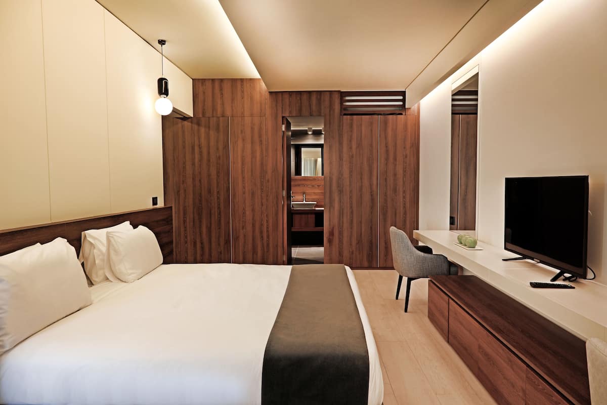 Quarto de hotel moderno com uma cama grande, escrivaninha, cadeira, televisão de tela plana e espelho.