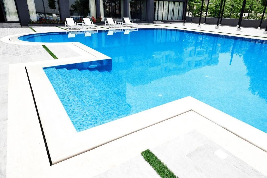 Piscina com espreguiçadeiras brancas e deck revestido de azulejos.