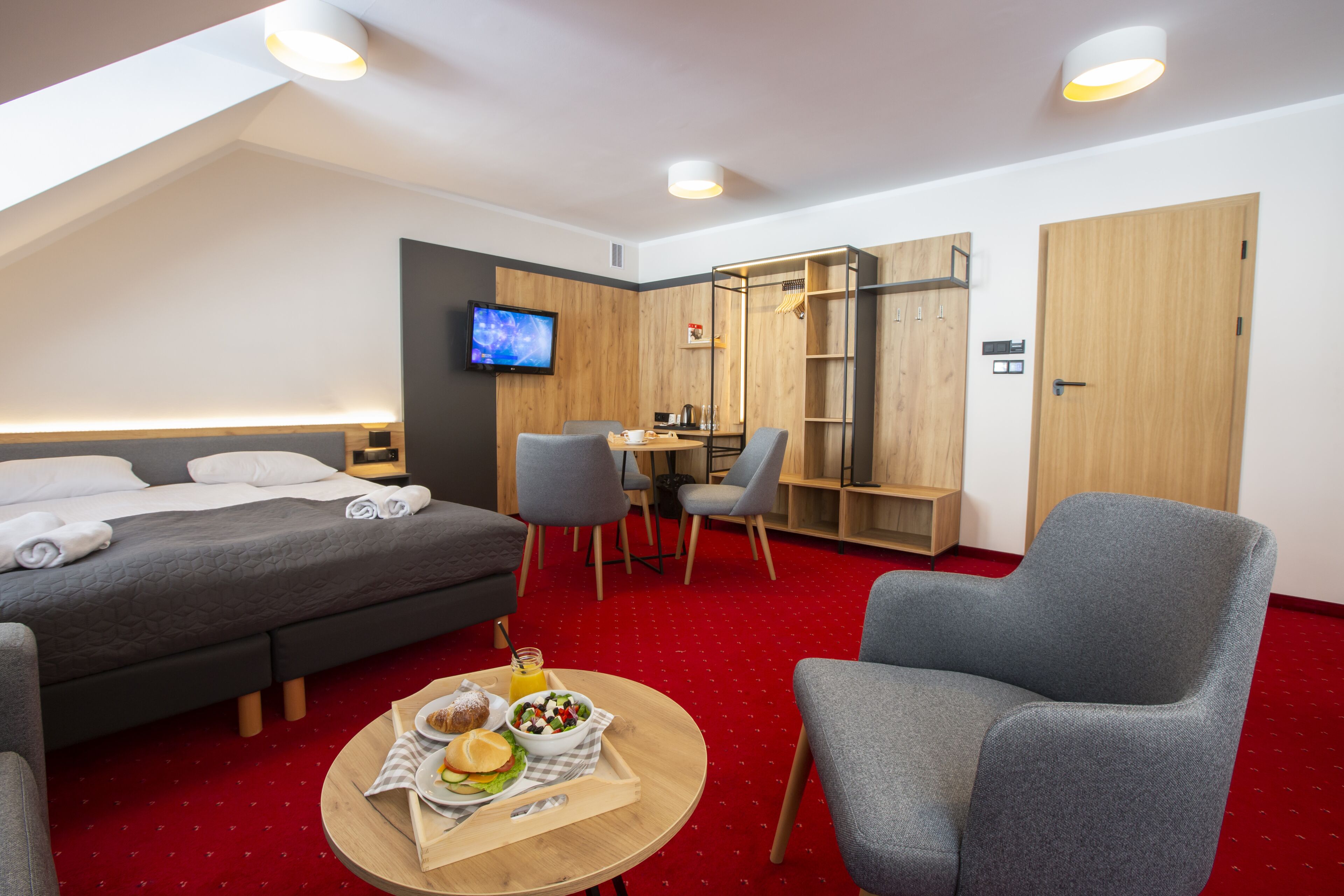 Quarto de hotel moderno com cama, mesa de jantar com café da manhã, televisão e área de trabalho.