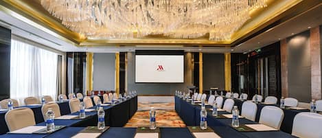 Sala de conferências com uma mesa comprida, garrafas de água e uma tela de projeção exibindo o logotipo da Marriott.
