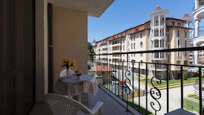 Uma varanda com uma mesa e cadeiras, um vaso de girassóis e vista para uma área residencial com edifícios altos.