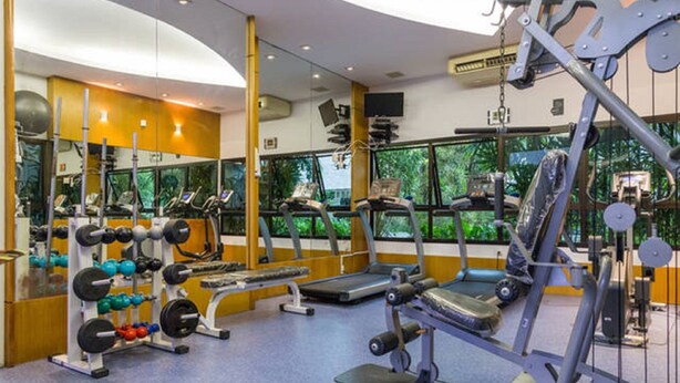 Uma academia com aparelhos de cardio, equipamentos de musculação e um espelho grande.
