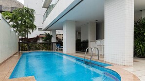 Piscina interior retangular com borda revestida em azulejo, rodeada por chão e paredes também em azulejo, e um corrimão de metal.