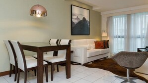 Uma área de refeições com uma mesa e cadeiras, um sofá branco, uma cadeira moderna e um quadro na parede.