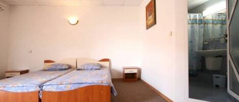 Quarto com uma cama de casal, mesas de cabeceira, uma pequena luminária e um banheiro visível através de uma porta de vidro.