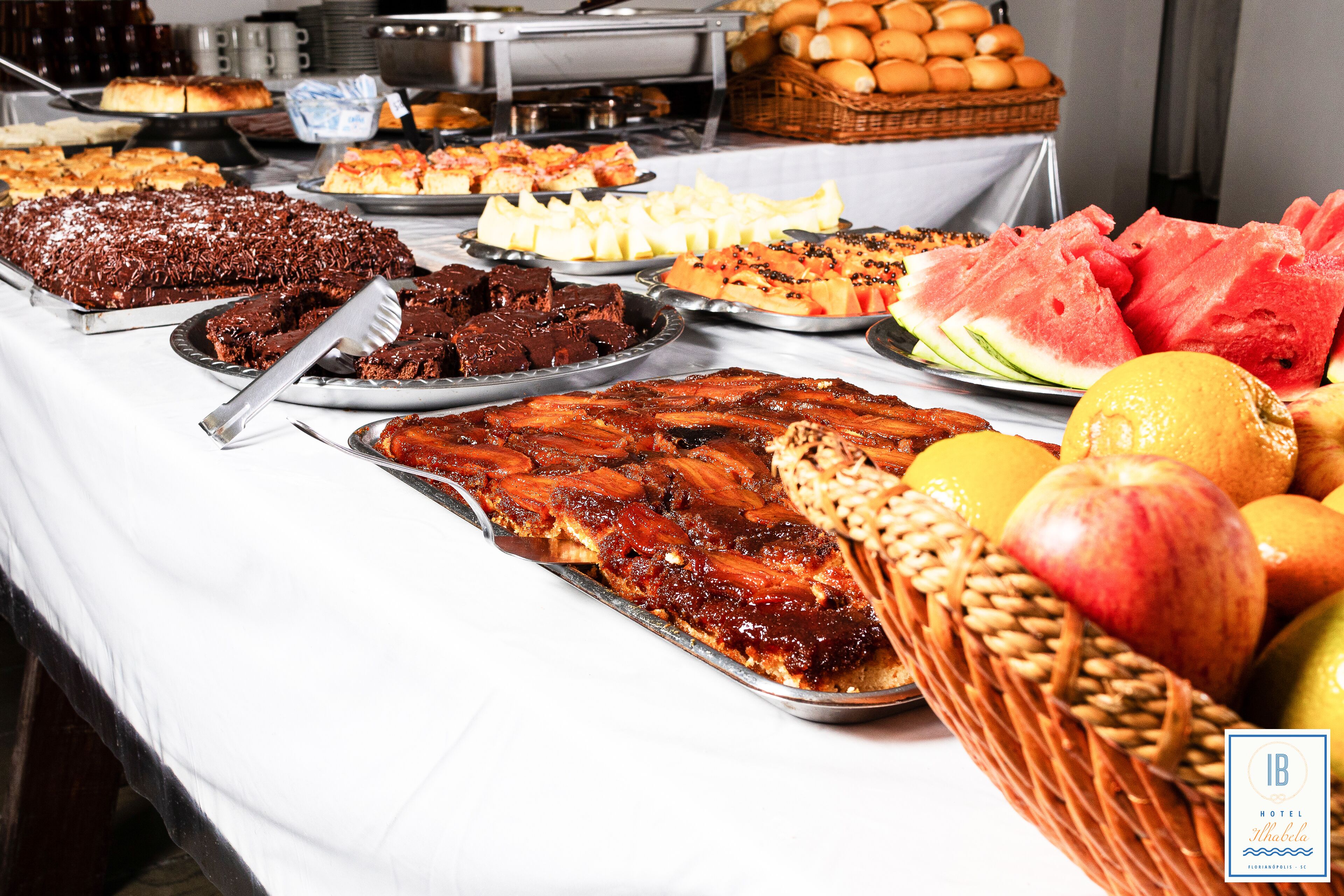 Buffet com diversas opções de comida, incluindo bolos, frutas e uma melancia.