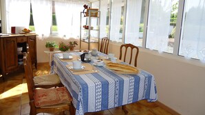 Uma área de refeições com uma mesa posta para dois, uma cafeteira, xícaras e uma cesta de pão.