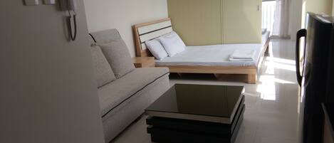 Quarto moderno com sofá, cama, TV e mesa de centro de vidro.