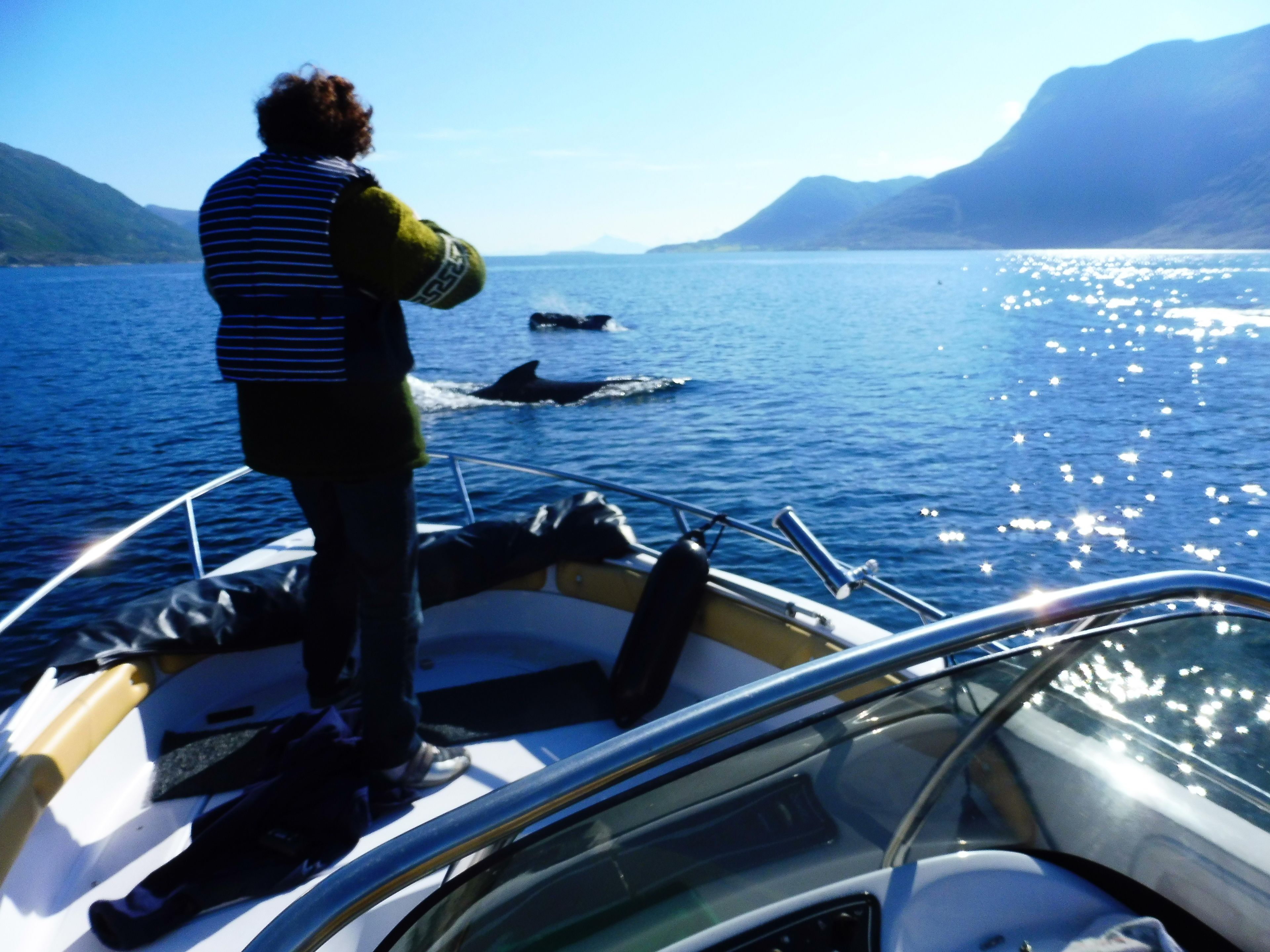 Uma pessoa num barco, com vista para o mar e montanhas ao fundo.