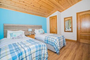 Quarto com duas camas, teto de madeira e parede azul.