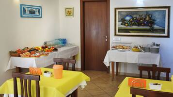 Uma sala de jantar com mesas preparadas para o café da manhã, apresentando diversos tipos de comida e um quadro na parede.
