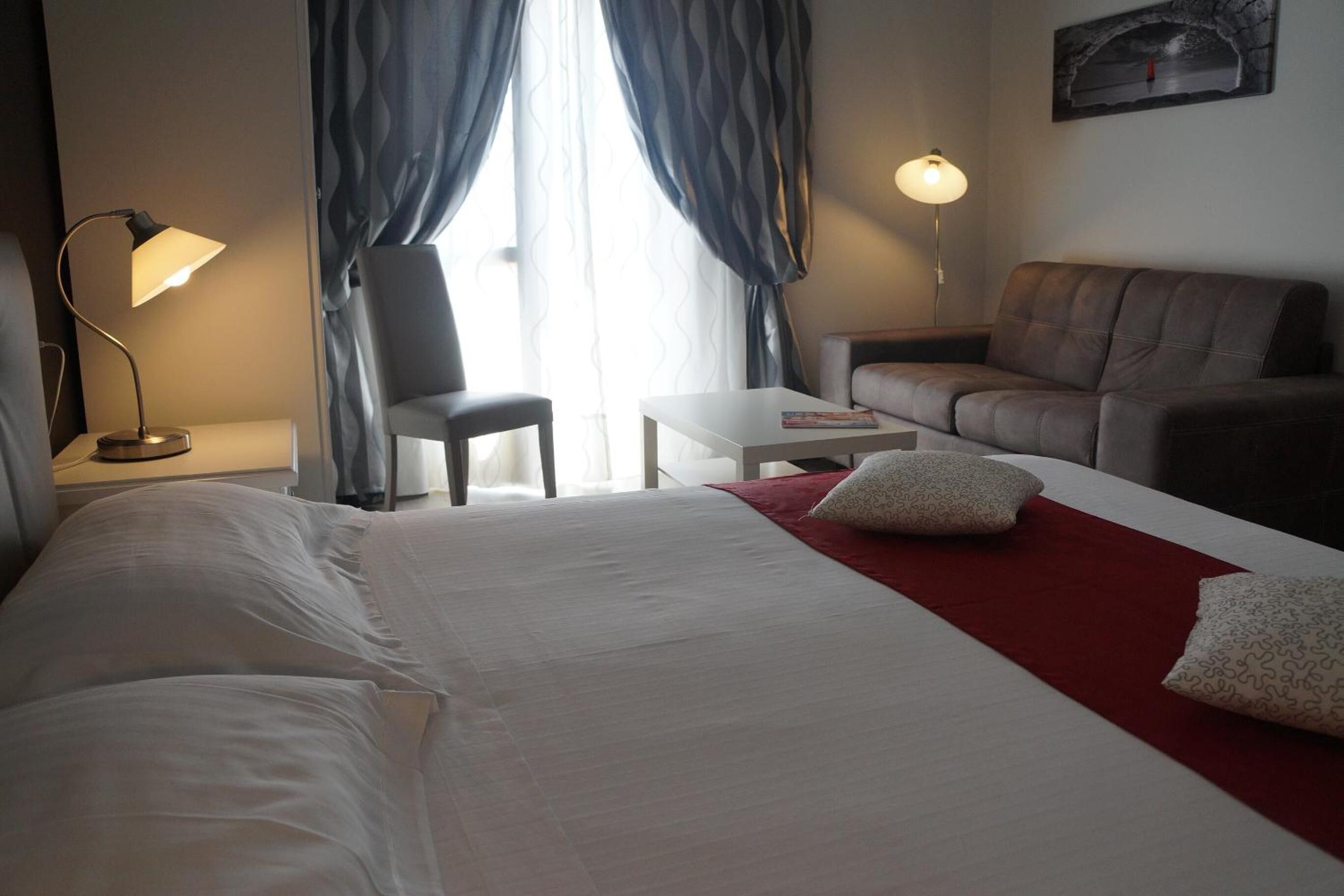 Quarto de hotel com uma cama grande, uma escrivaninha, um sofá e duas luminárias.