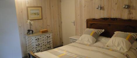 Quarto com cabeceira de madeira, cama com roupa de cama listrada, mesa de cabeceira com abajur e cômoda com espelho.