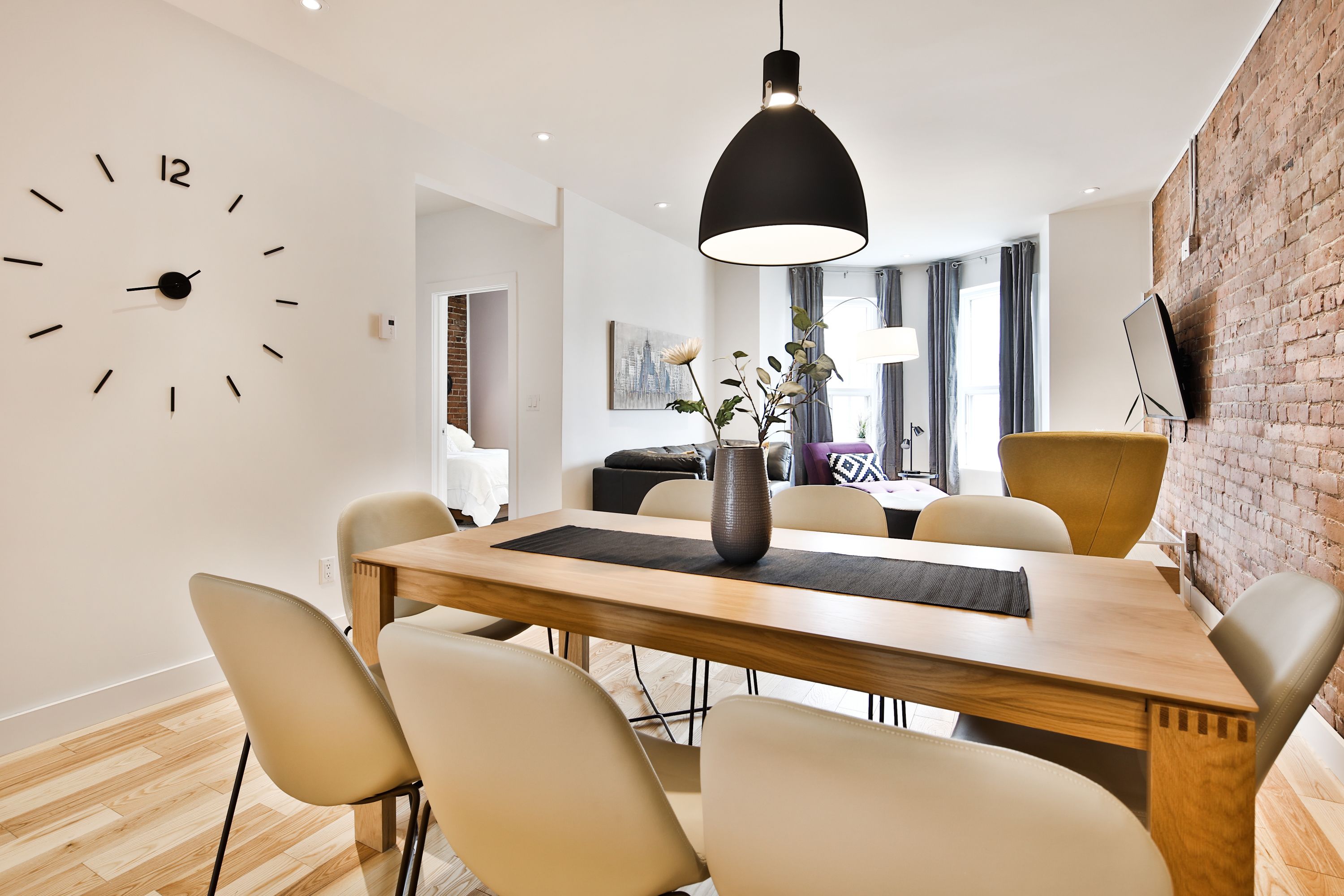 Uma sala de jantar moderna com mesa de madeira, cadeiras bege e luminária pendente preta.