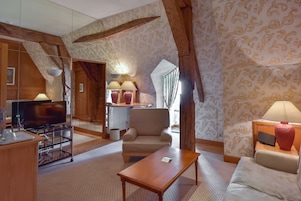 Quarto de hotel acolhedor com teto de madeira, sofá confortável, mesinha e televisão sobre um móvel.