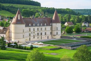Um castelo com duas torres imponentes, um pátio com piscina e um jardim bem cuidado.
