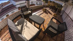 Um pátio iluminado pelo sol, com móveis de vime, uma mesa pequena e um vaso de planta.