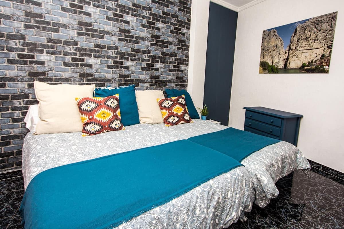 Quarto com parede de tijolos, cama com roupa de cama estampada, parede azul de destaque e pintura de um cânion.