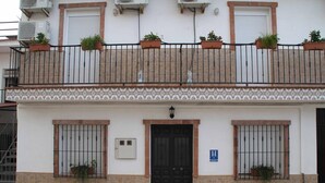 Um edifício com porta preta, duas janelas com grades de metal e uma varanda com plantas em vasos.