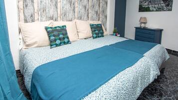 Uma cama com colcha e almofadas estampadas, cabeceira de madeira, mesa de cabeceira pequena com abajur e um quadro pendurado na parede.