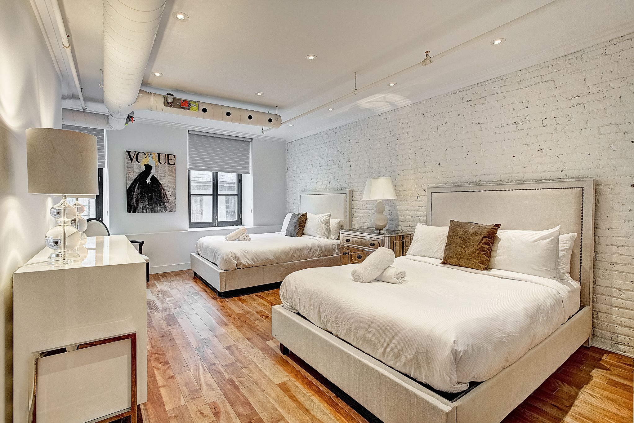 Quarto moderno com duas camas, uma escrivaninha e uma janela grande.