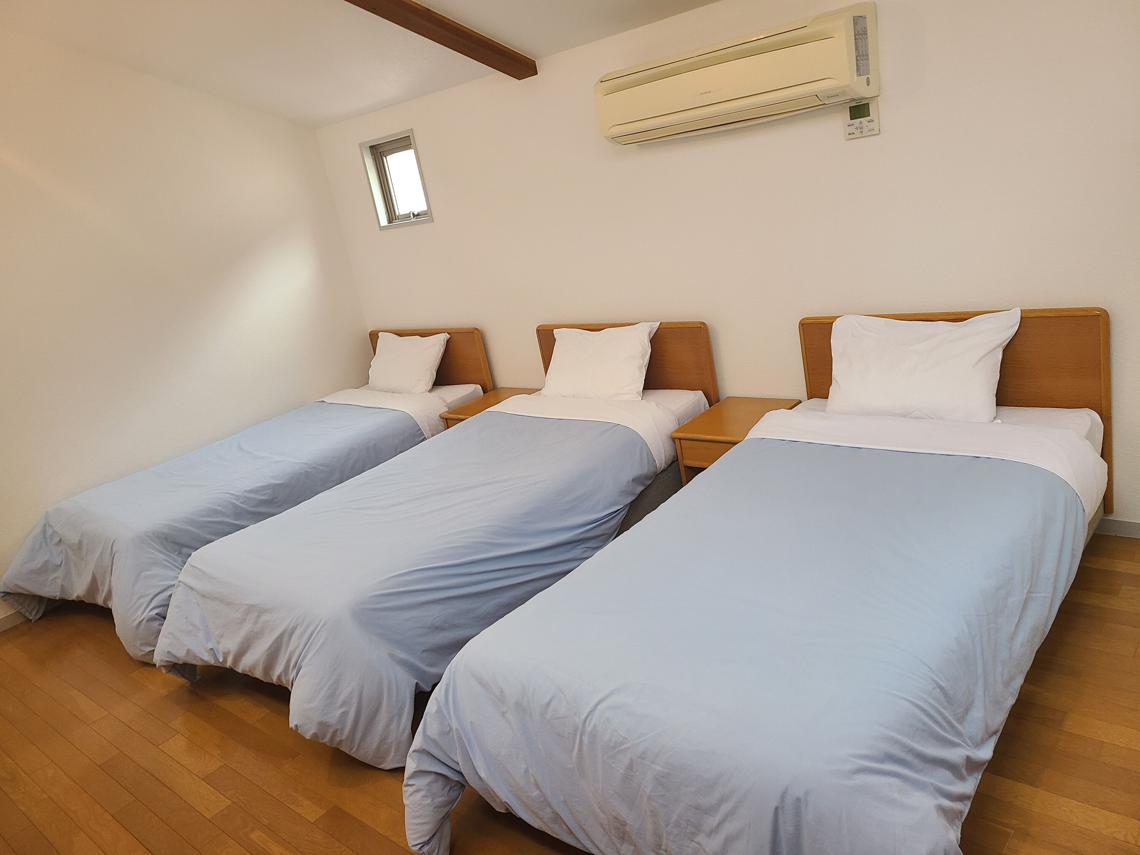 Quarto com três camas de solteiro, uma pequena janela e um aparelho de ar condicionado.