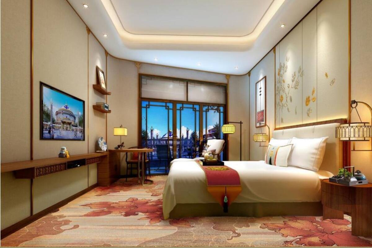Quarto de hotel com uma cama grande, uma escrivaninha, uma cadeira e vista para o horizonte urbano pelas janelas.