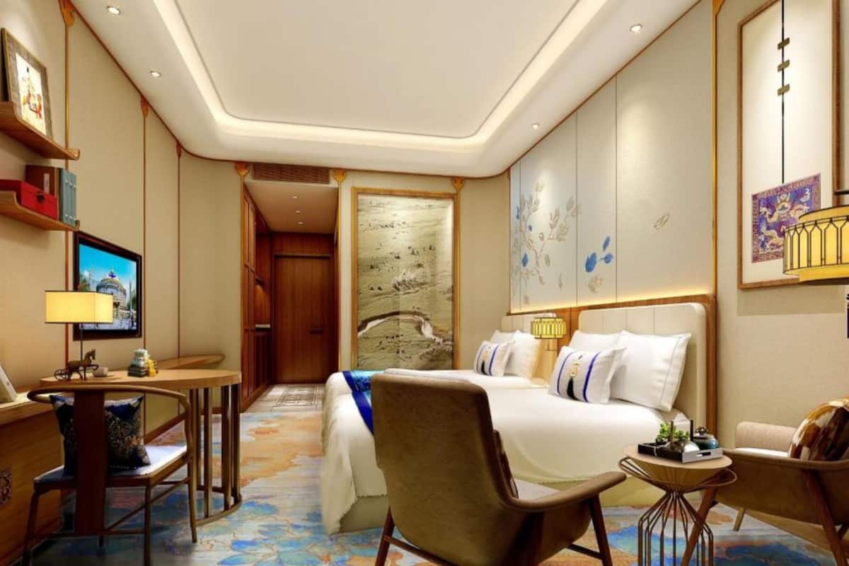 Quarto de hotel com uma cama, escrivaninha, cadeira, mesa pequena e televisão.