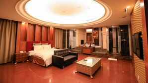 Quarto de hotel com uma cama grande, um sofá, uma mesa de centro, um banheiro com pia e espelho, e um chuveiro.