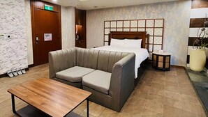 Quarto de hotel com cama, sofá, mesinha e planta em vaso.