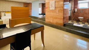 Quarto de hotel moderno com área de jantar, cabeceira de madeira, piso xadrez e vista para a cidade.