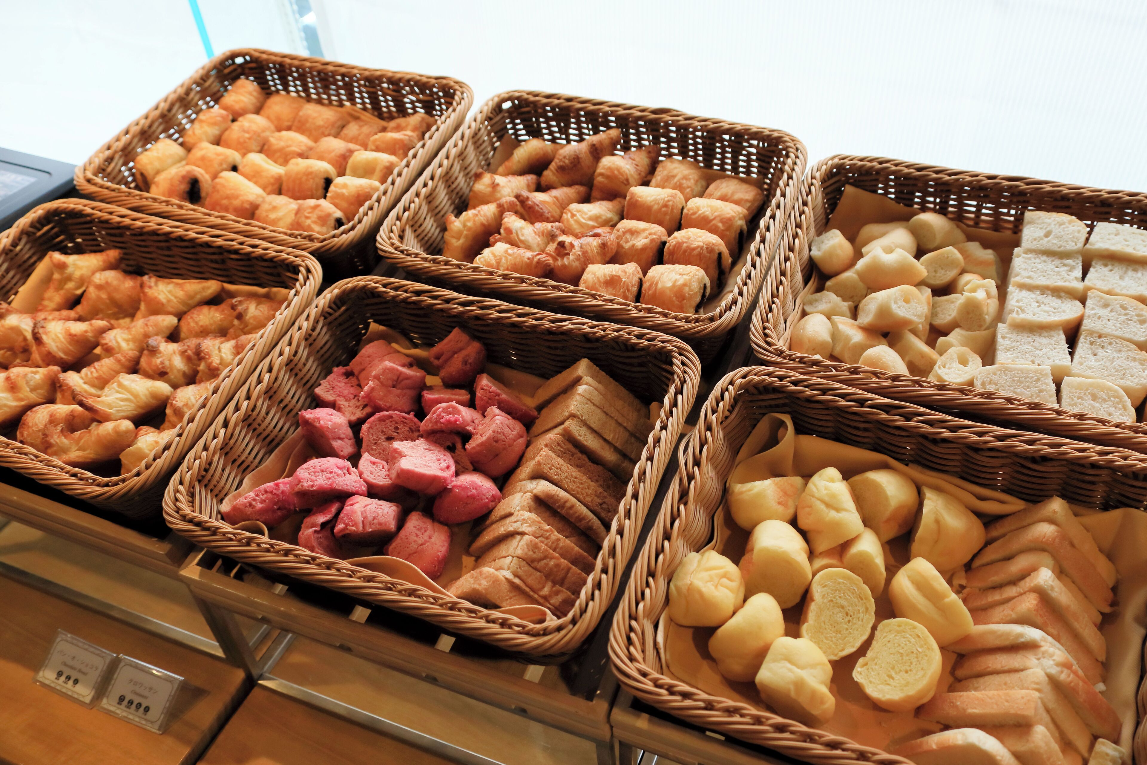 Exposição de pães e doces numa padaria, com diferentes tipos em cestos de vime.