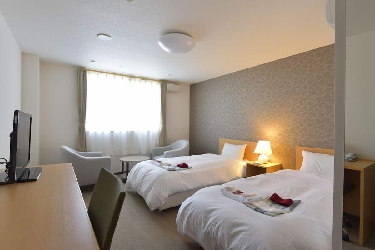 Quarto de hotel com duas camas, uma escrivaninha, uma cadeira, um abajur e uma televisão.