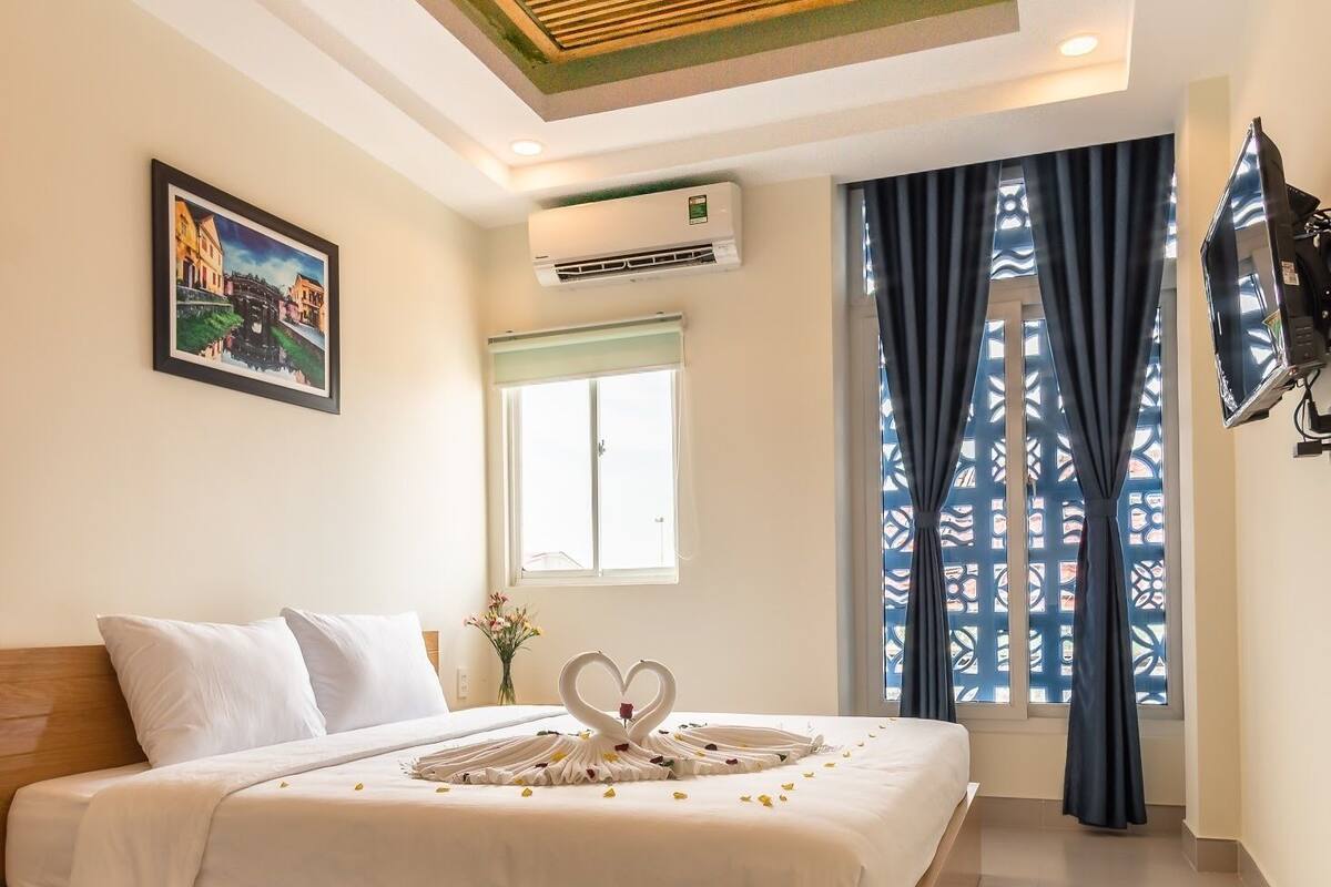 Quarto com cama de madeira, ventoinha no teto, televisão na parede e janela com cortinas estampadas.