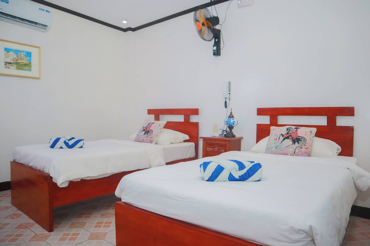 Quarto de hotel com duas camas de madeira, roupa de cama branca e uma pequena mesa de cabeceira com uma lâmpada.