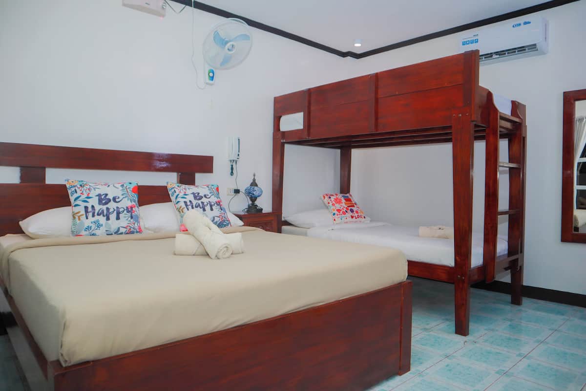 Quarto com uma cama beliche de madeira e uma cama de solteiro, ambos com roupa de cama branca e almofadas decorativas.