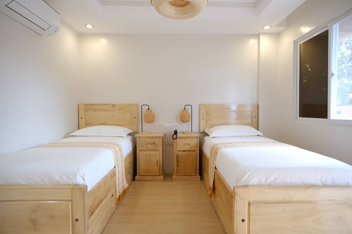 Quarto duplo com duas camas de madeira, mesas de cabeceira e uma janela.