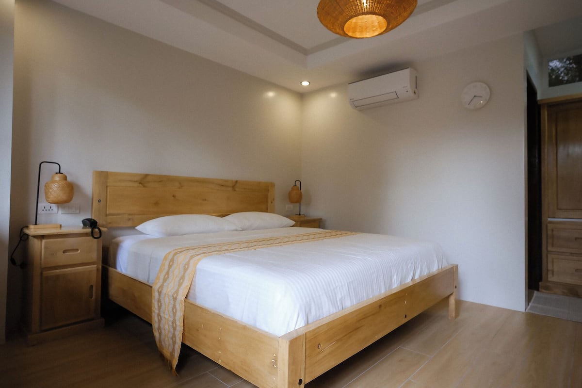 Quarto com cama de madeira, mesas de cabeceira, relógio de parede e ar condicionado.