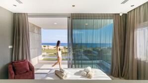 Quarto de hotel moderno com uma cama grande, uma cadeira vermelha e uma varanda com vista para o oceano.