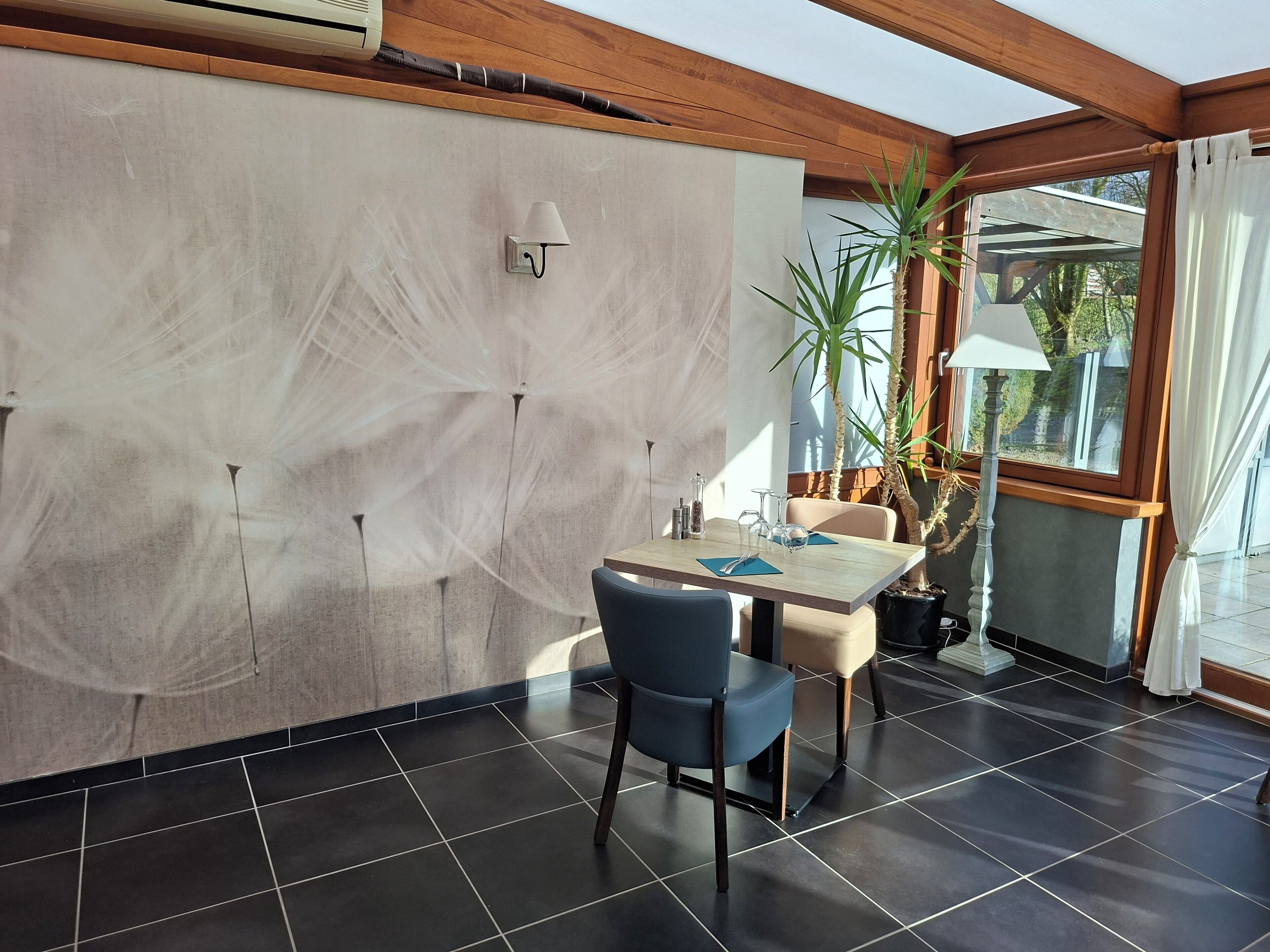 Uma sala de jantar moderna com teto de madeira, uma janela grande com cortinas, uma planta em vaso e uma mesa posta para dois.