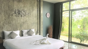 Quarto com uma cama grande, um objeto decorativo na parede, um relógio e vista para o verde lá fora.