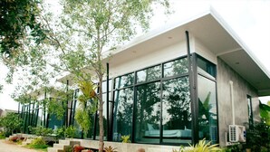 Um edifício moderno com grandes janelas de vidro, fachada de concreto e um jardim paisagístico com degraus que levam à entrada.