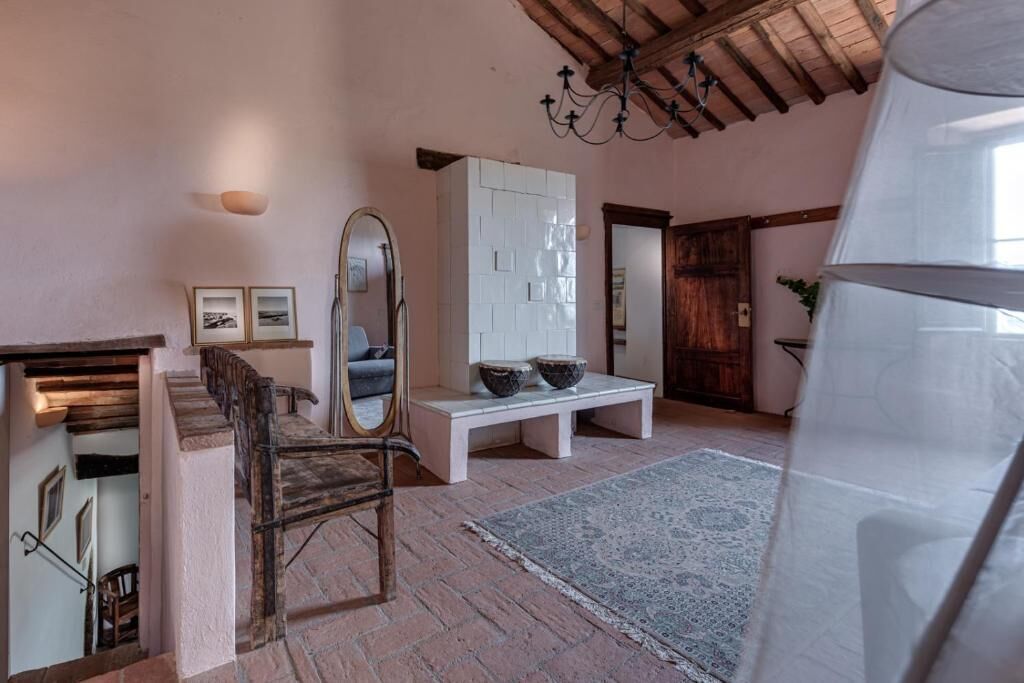 Um interior rústico com soalho de pedra, mobiliário de madeira, um banco branco e um espelho grande.