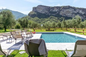 Uma piscina com espreguiçadeiras e um deck de madeira, cercada por vegetação e ao fundo, uma montanha.