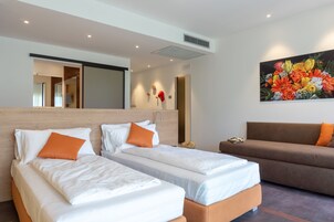 Quarto de hotel com duas camas, um sofá, um quadro floral grande e um espelho na parede.
