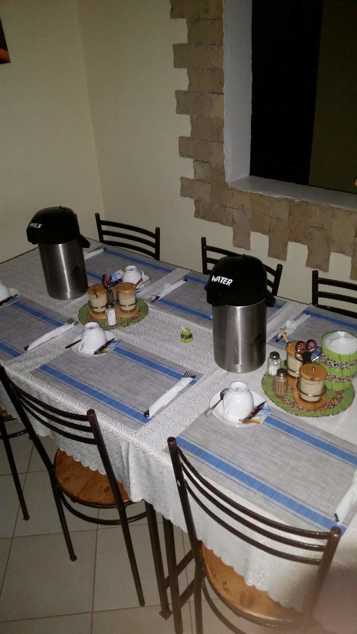 Mesa de jantar posta com toalha branca, duas garrafas de água de aço inoxidável e diversos pratos e talheres.